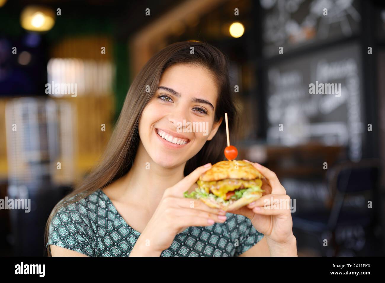 Happy woman looking at you showing burger in a bar interior Stock Photo ...