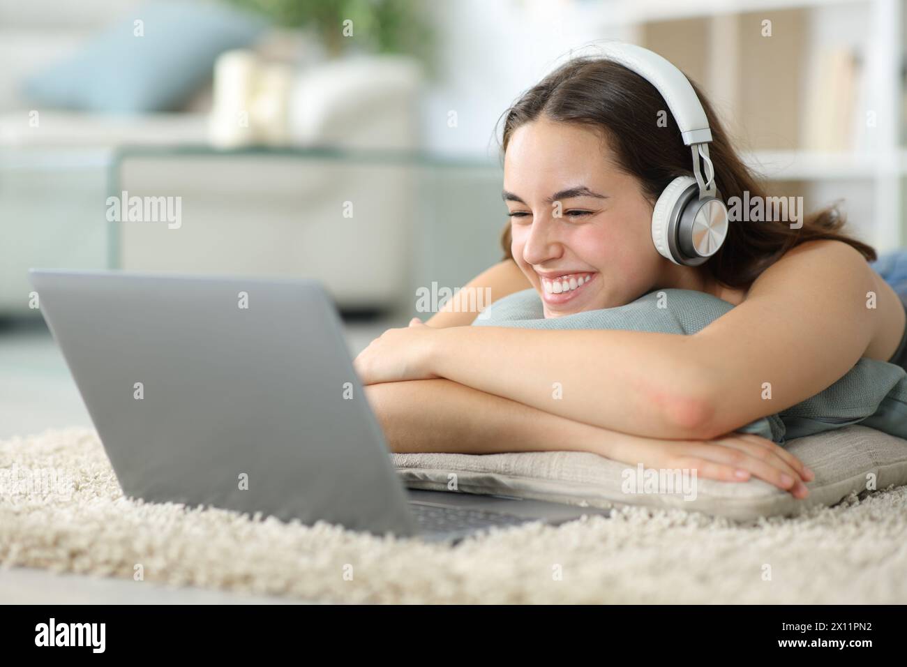 Happy woman watching media content on laptop lying on a carpet at home ...