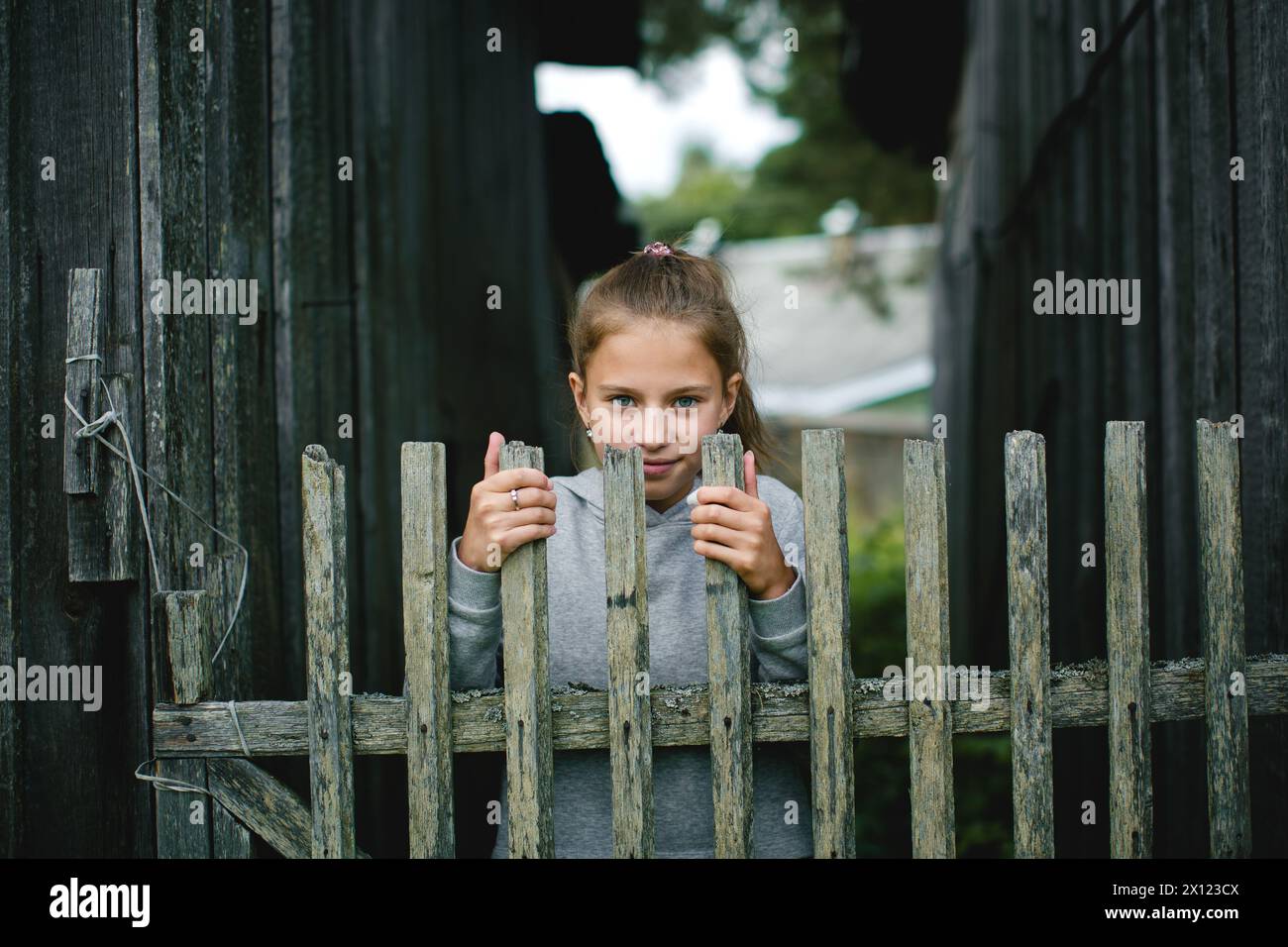 A teenage girl by a wooden fence, her face expressing quiet ...