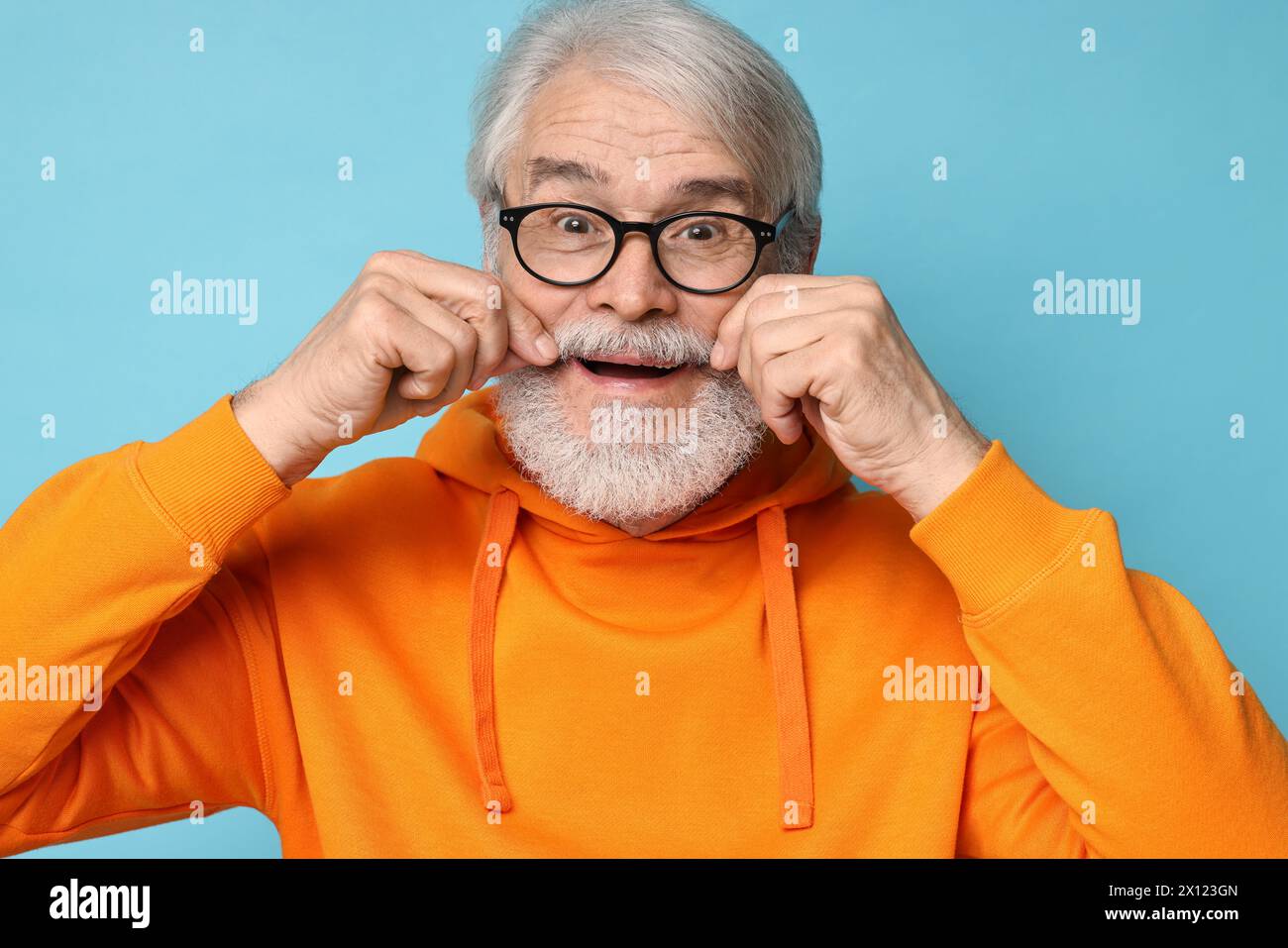 Senior man touching mustache on light blue background Stock Photo - Alamy
