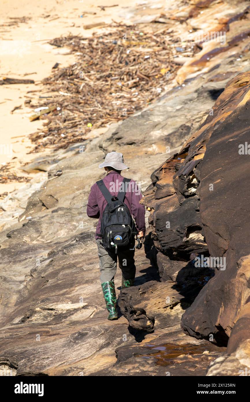 Rear view australian man walking along beach rocks with fishing rod to ...