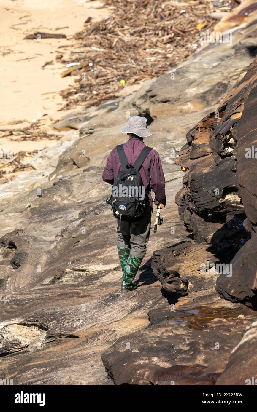 Rear view australian man walking along beach rocks with fishing rod to ...