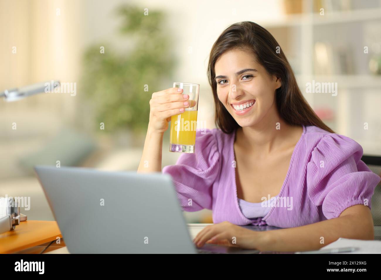 Happy student holding orange juice sitting at home Stock Photo - Alamy