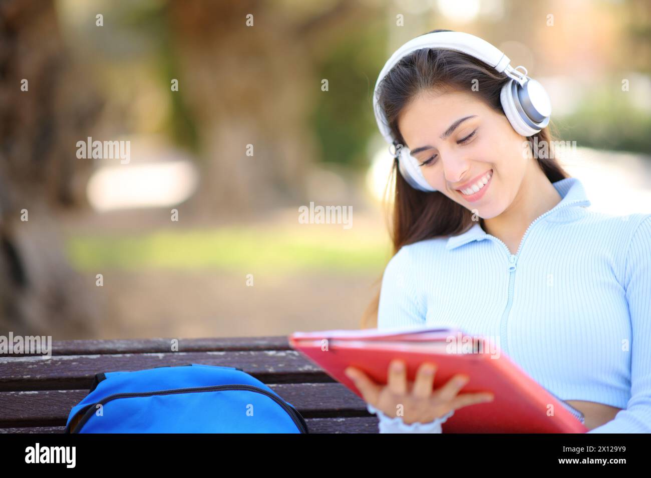 Happy student in a park listening audio guide wearing headphone and ...