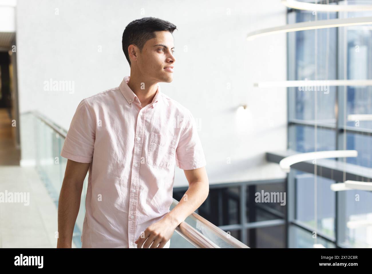 A young biracial man leaning on railing, looking to side in a modern ...