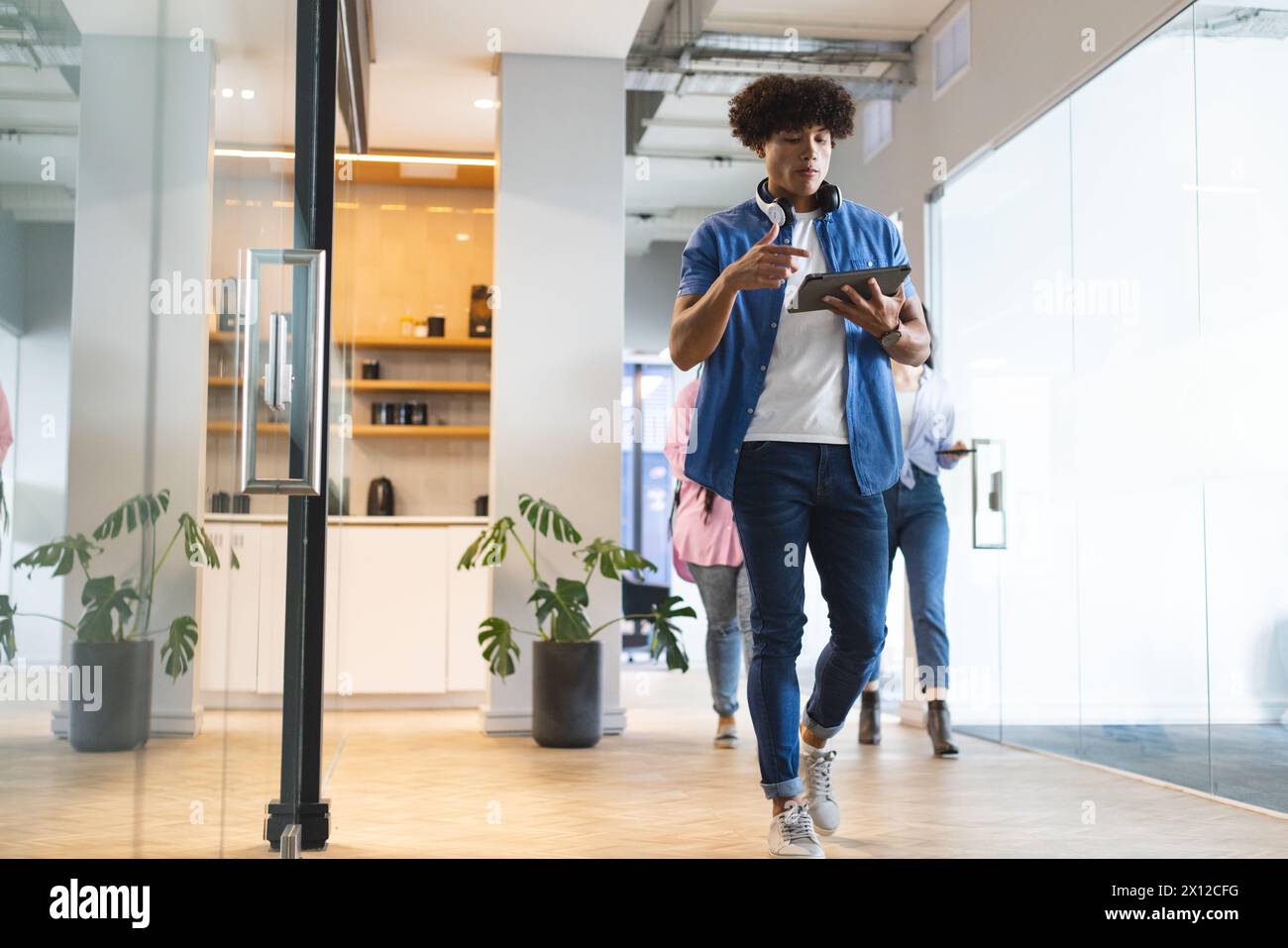 Young biracial man walking, using tablet and drinking coffee in a ...