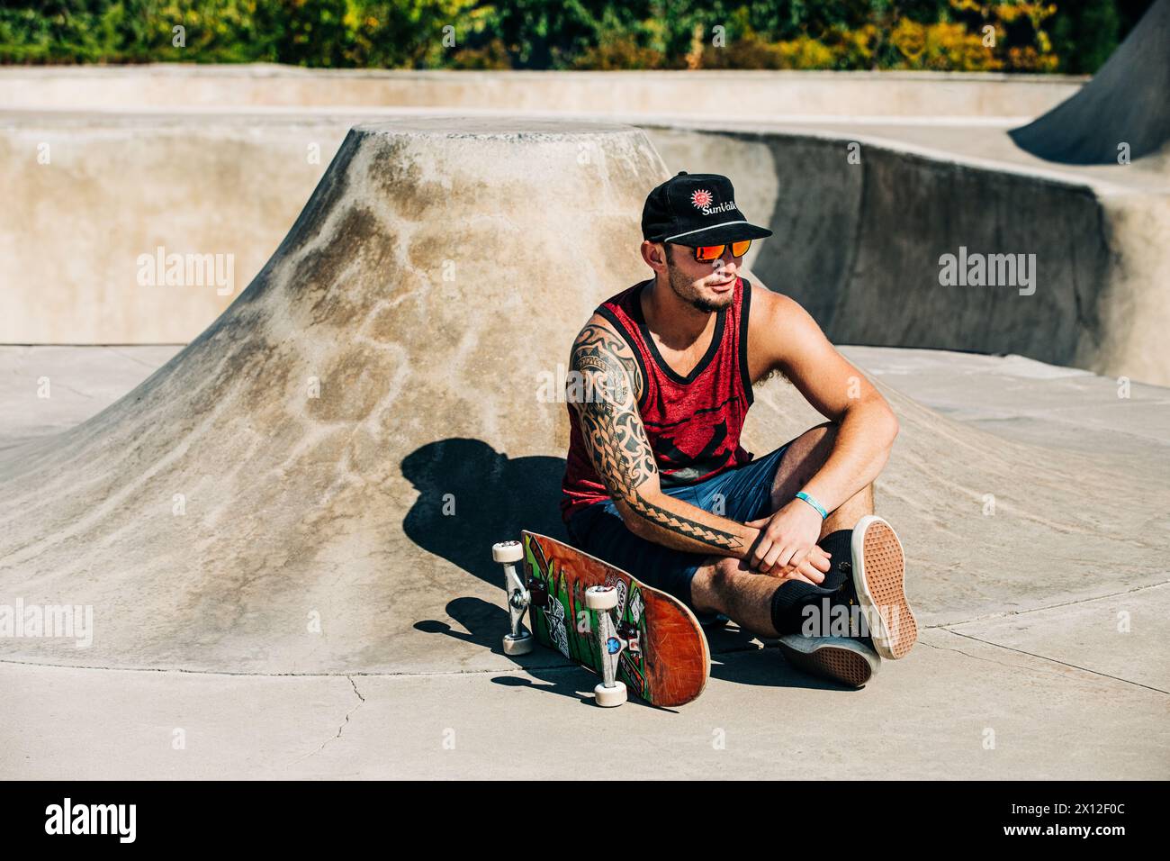 Skateboarder sitting on ground at skate park in the sun Stock Photo - Alamy