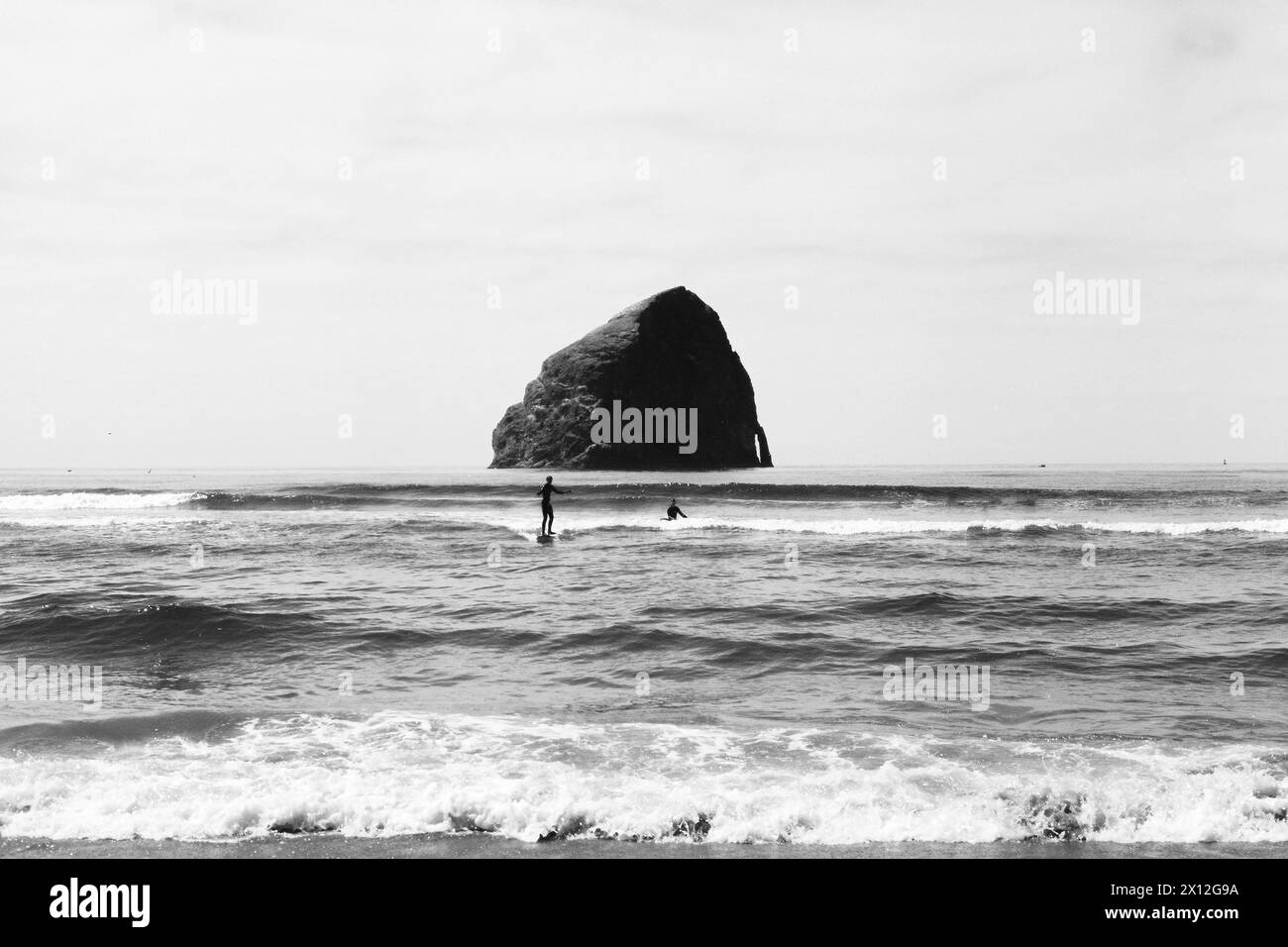 Surfers catching a wave in front of Haystack Rock in Oregon Stock Photo ...