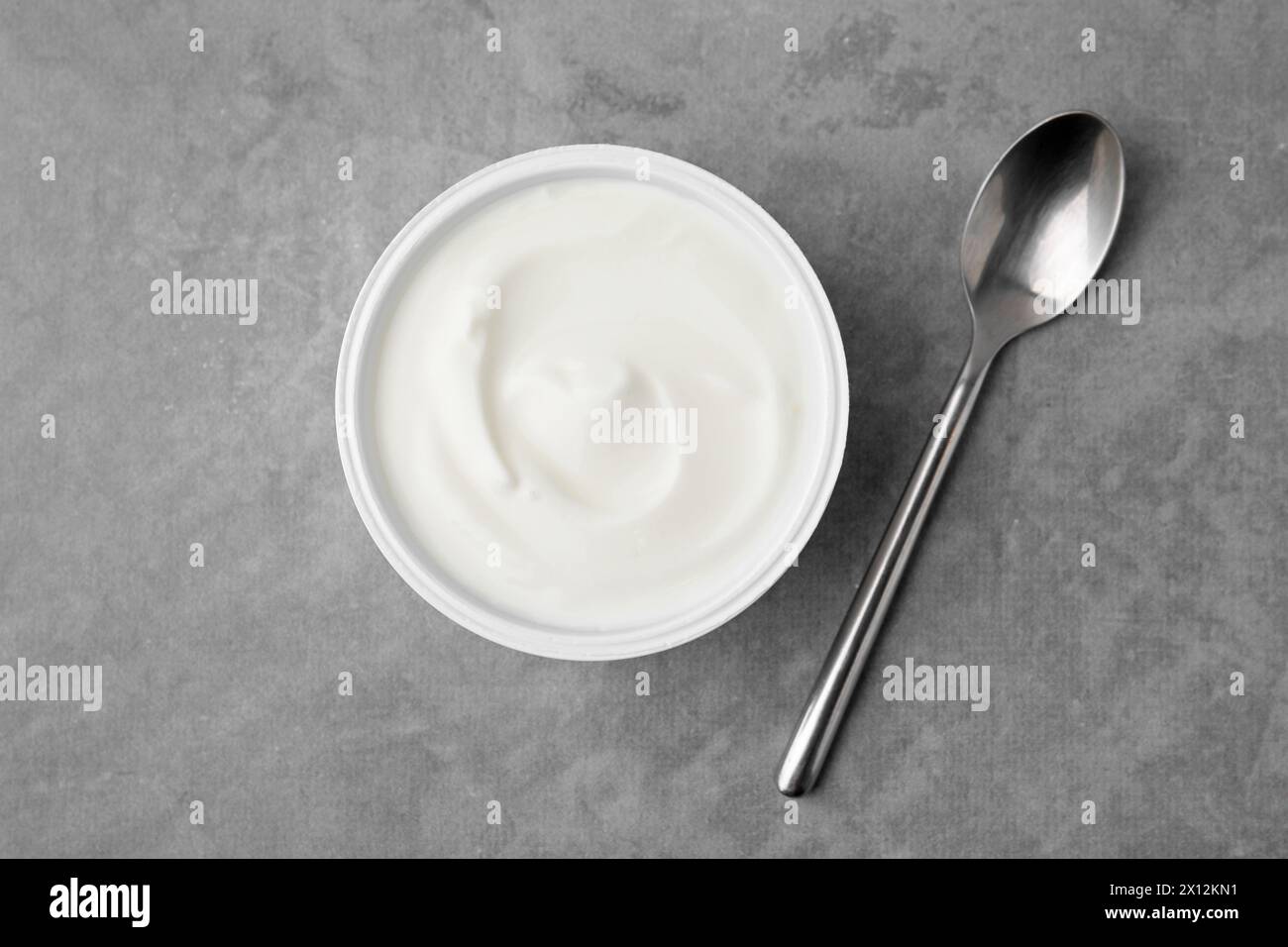 Delicious natural yogurt in plastic cup and spoon on grey table, top ...