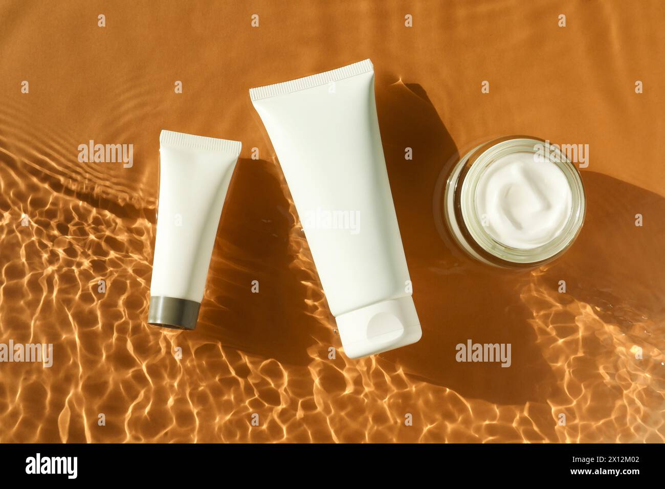 Tubes and jar with moisturizing cream in water on orange background ...