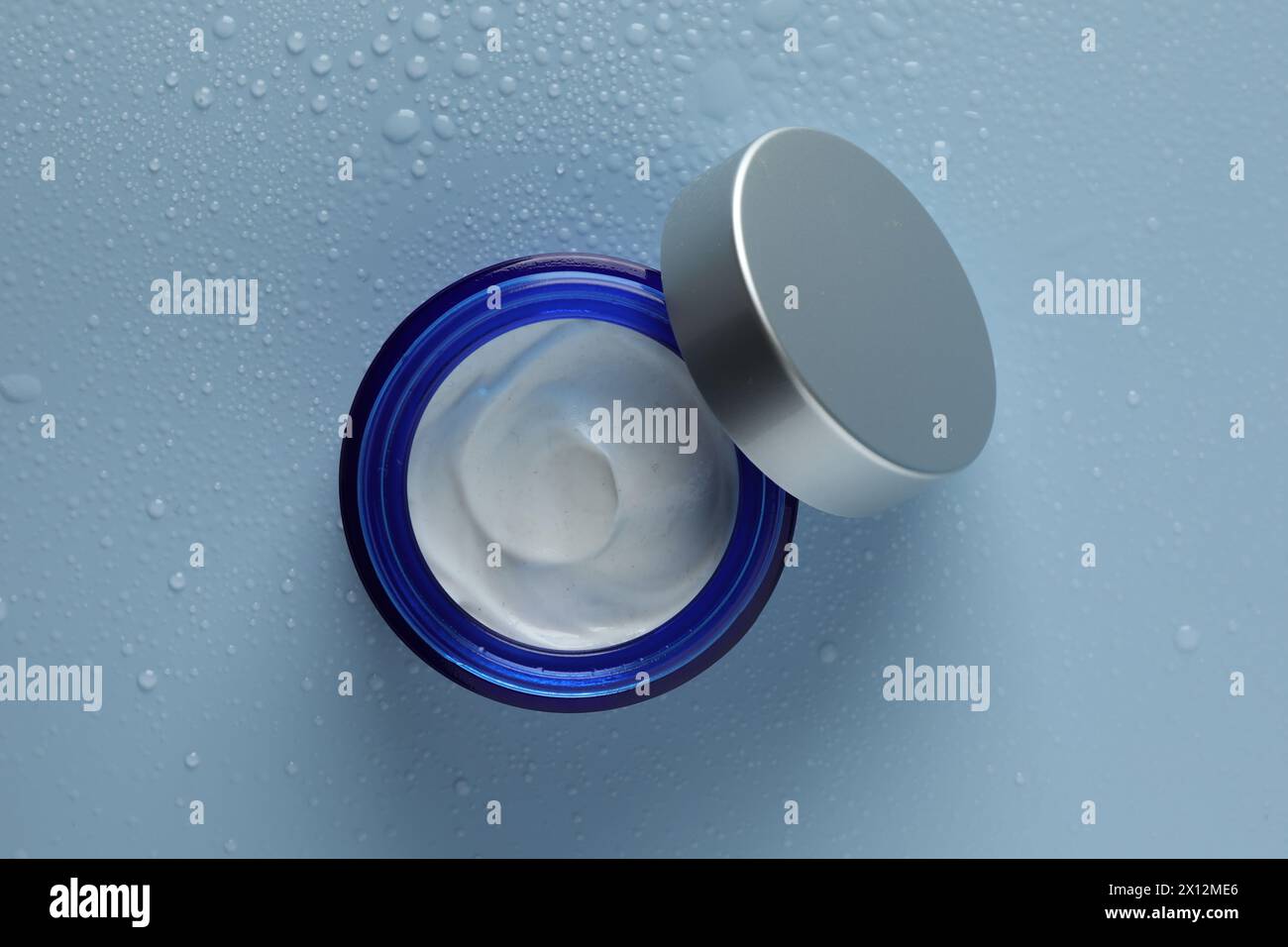 Moisturizing cream in open jar on light blue background with water ...