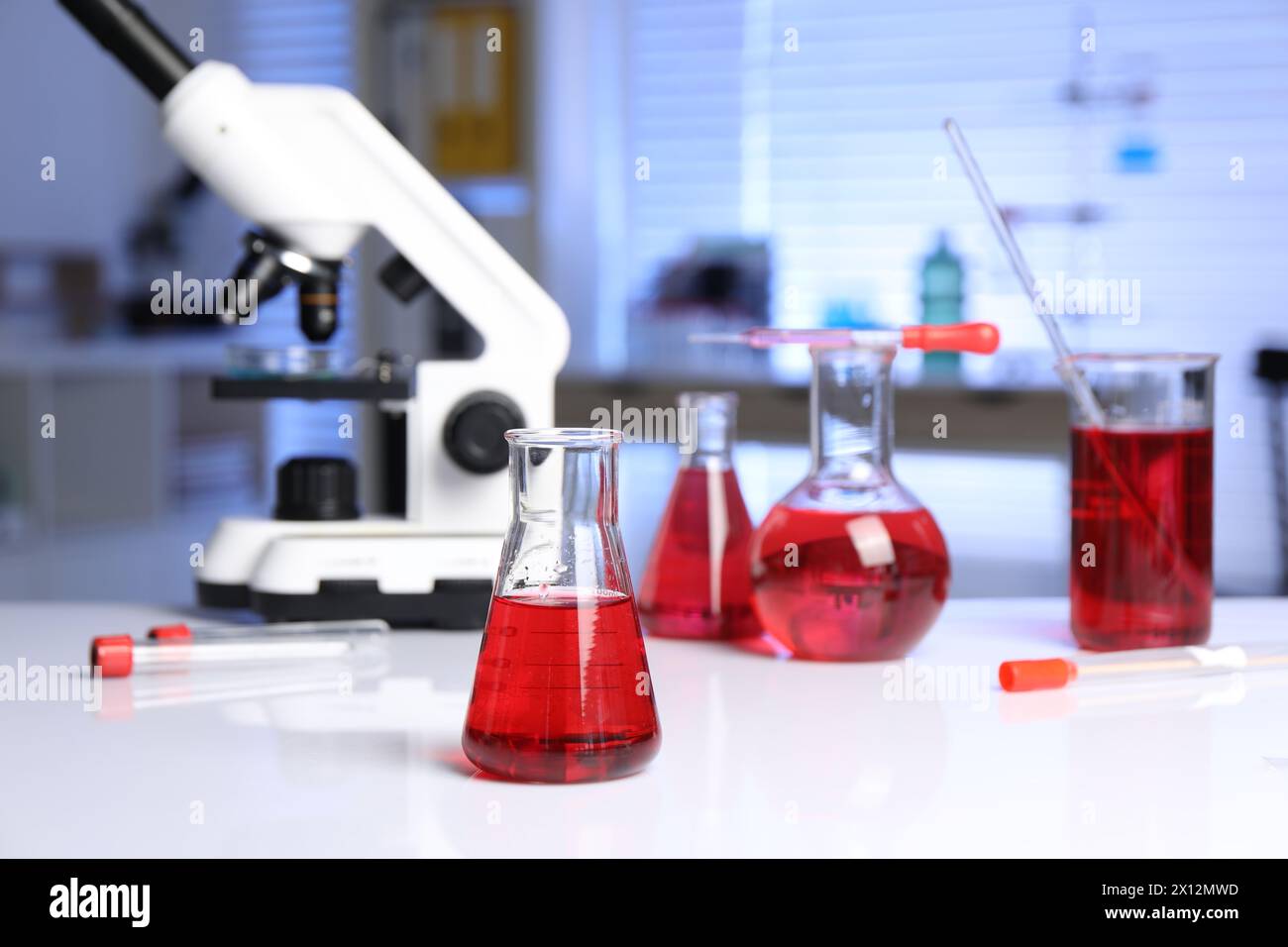 Laboratory analysis. Glass flasks with red liquid and microscope on ...