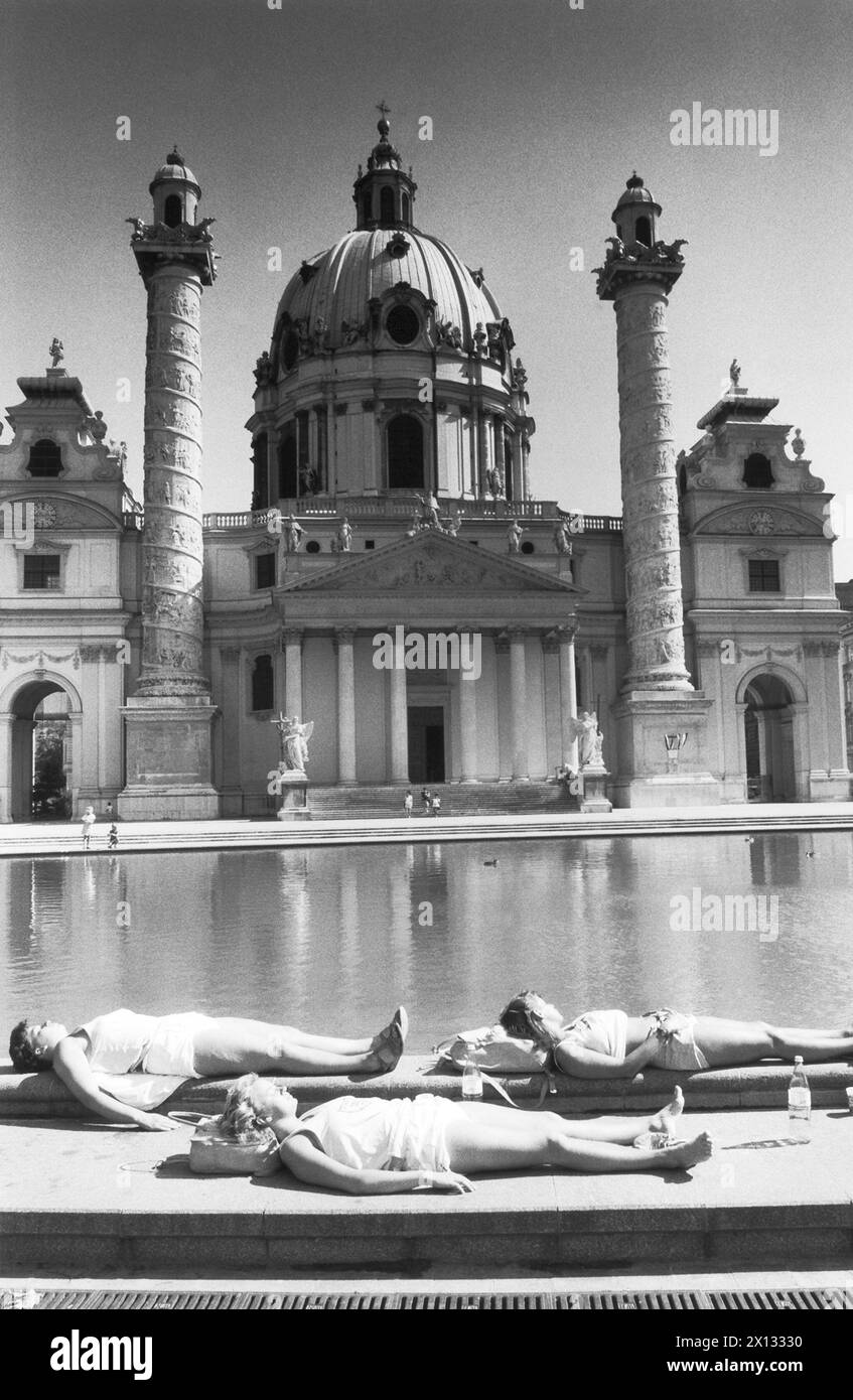 Three tourists make a sun bath in front of Karl's Cathedral in Vienna ...