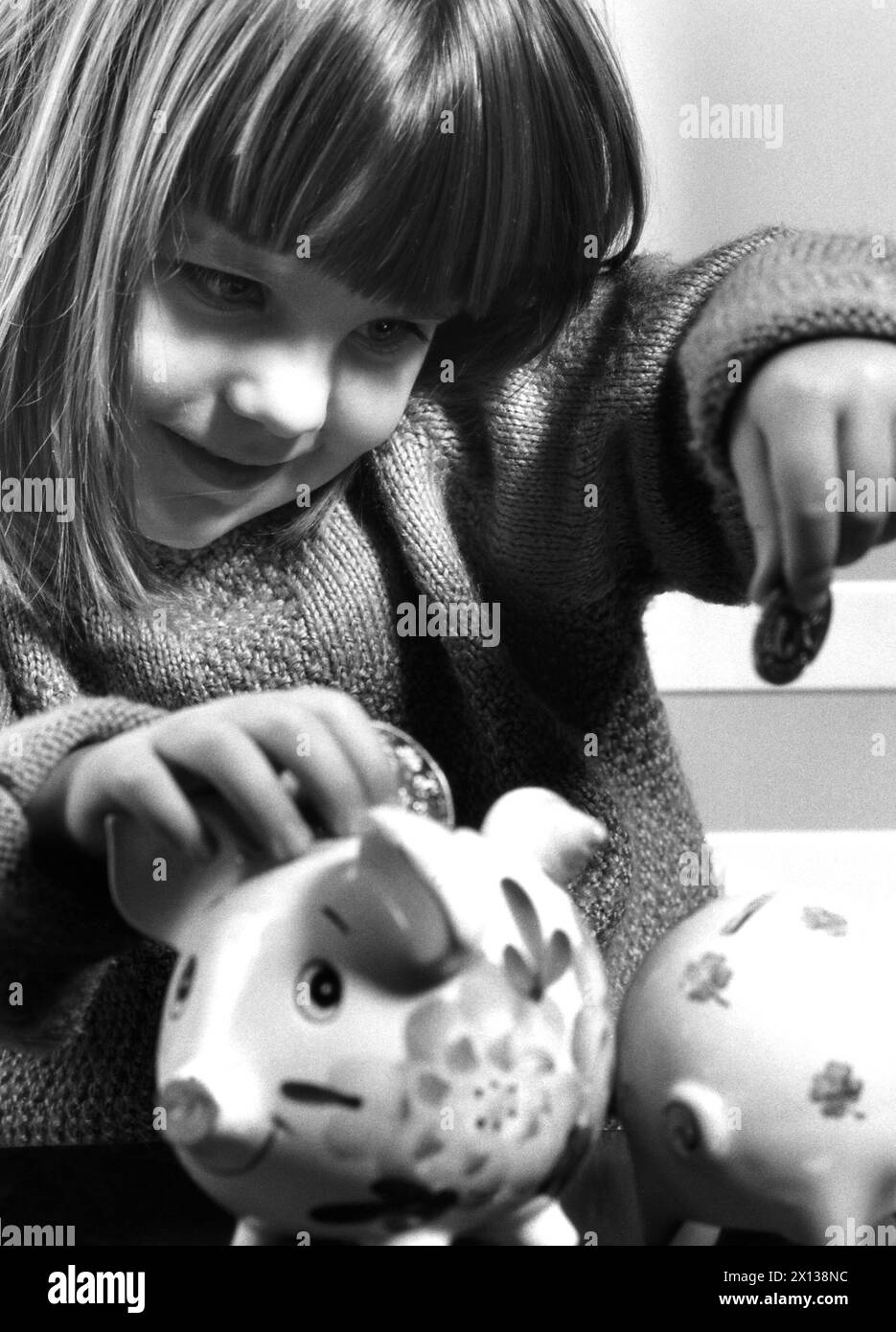A 4-year old girl puts some coins into her two piggy banks, captured on ...