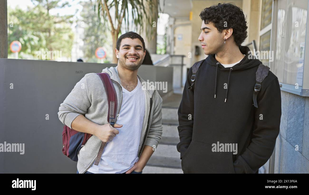 Two young men friends smiling and conversing on an urban city street ...