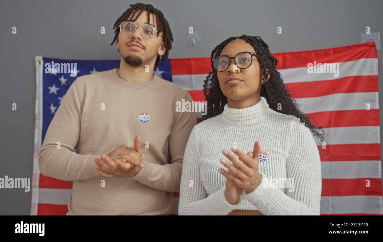A young man and woman with 'i voted' stickers, clapping before an ...