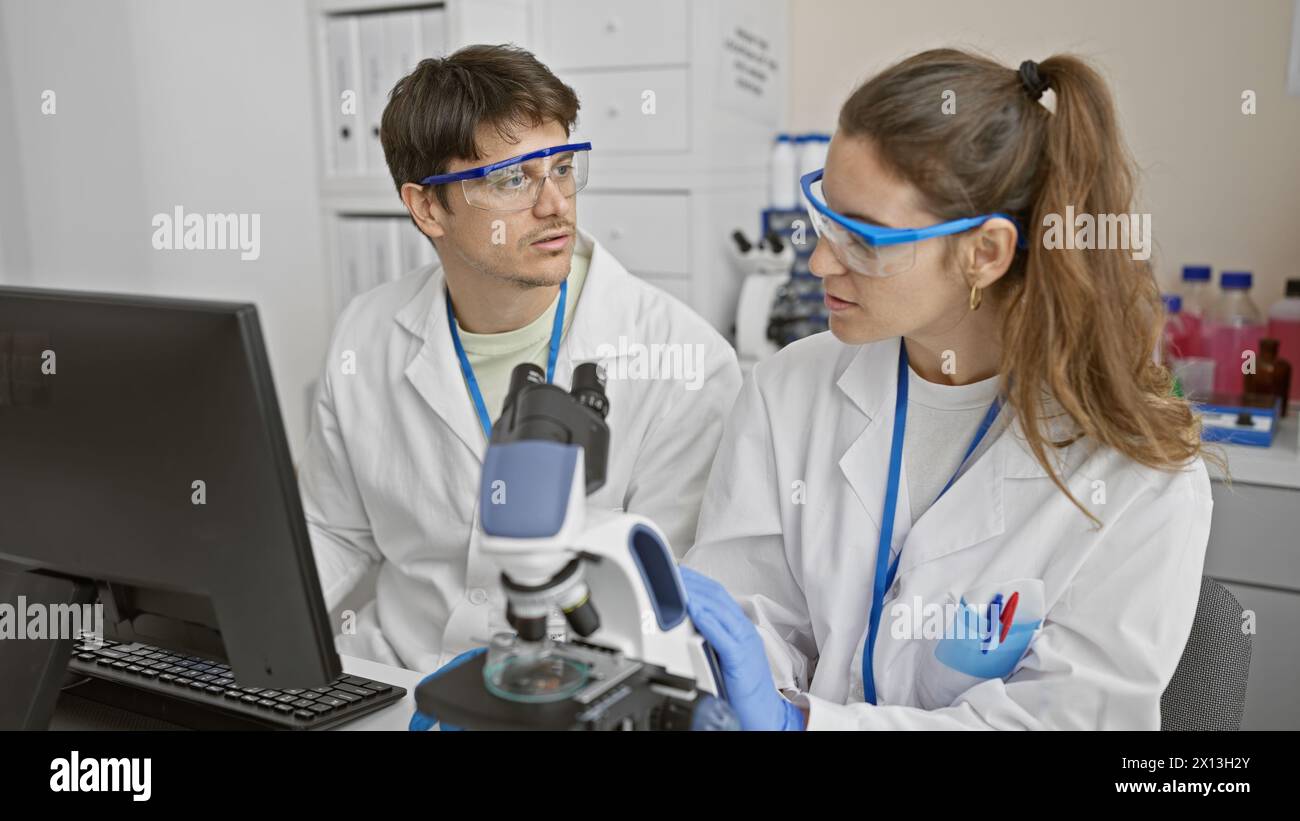 In a laboratory, a man and woman in lab coats and safety glasses ...