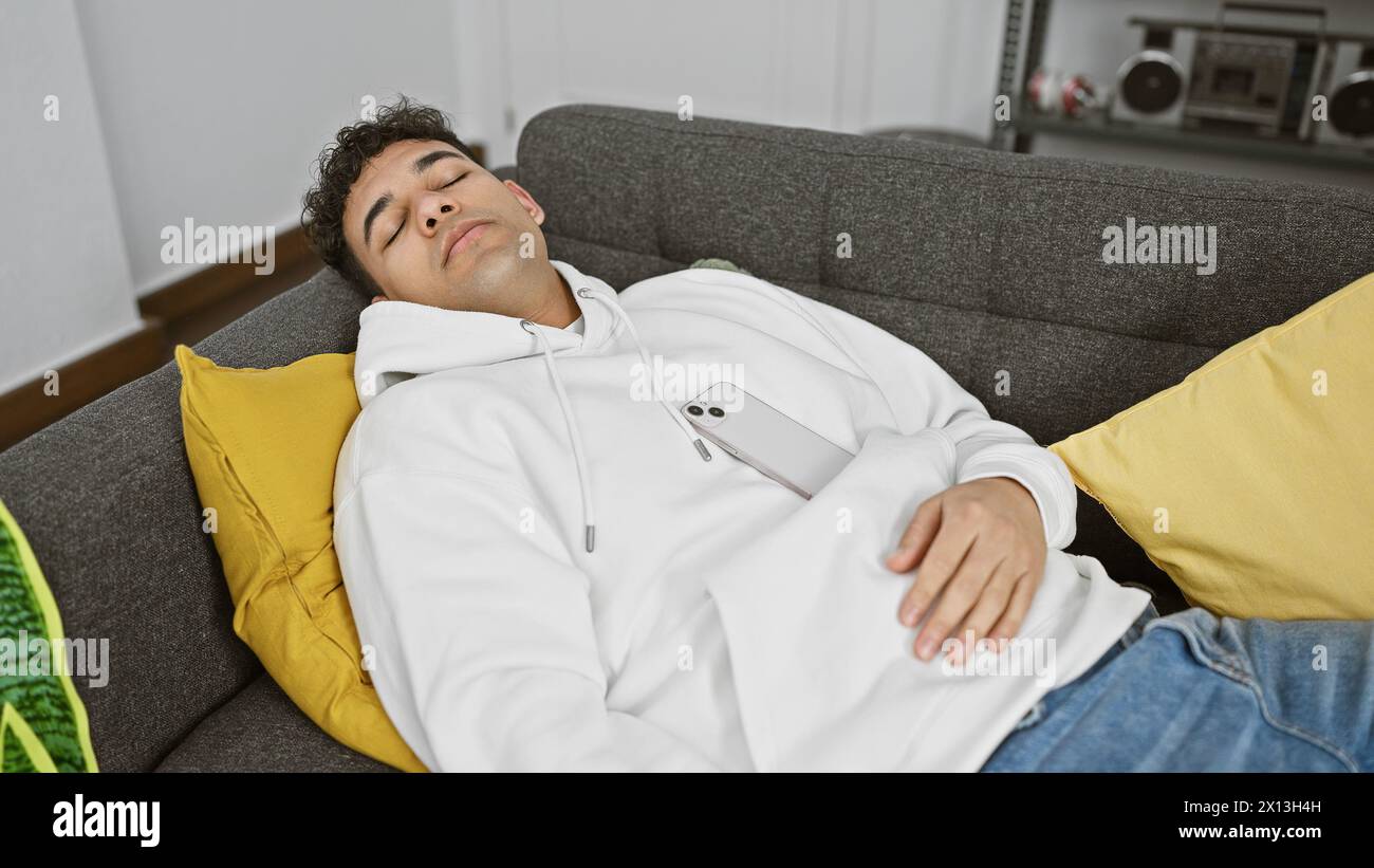 A relaxed young man sleeping on a gray couch with a yellow pillow and a ...