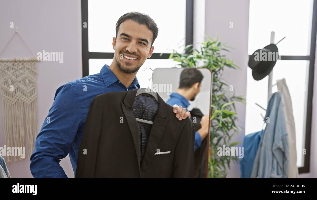 Handsome hispanic man smiling holding suit in a modern wardrobe room ...