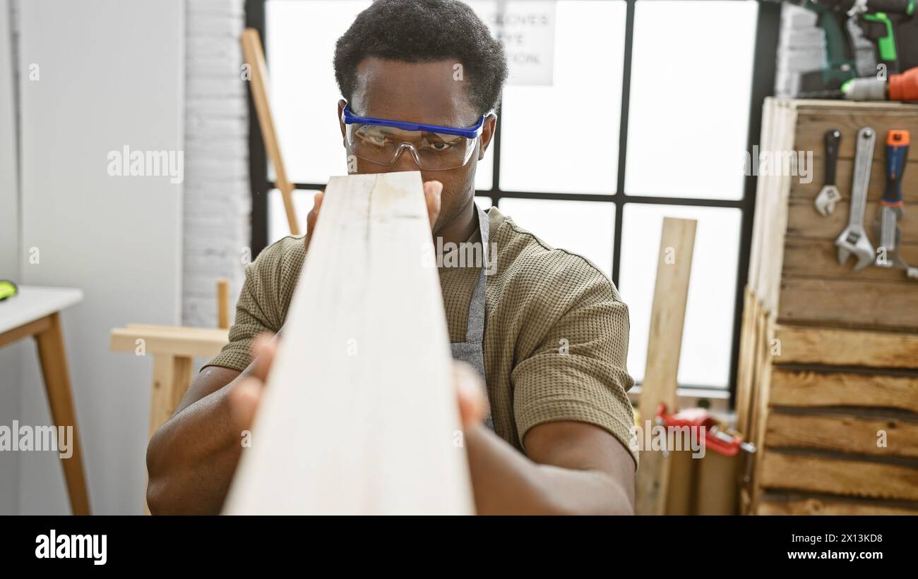 A young african american man wearing safety goggles inspects a plank of ...