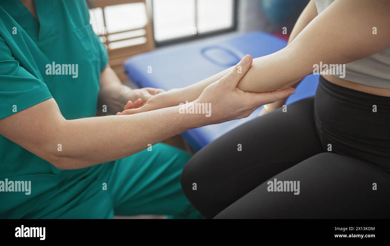 A physiotherapist in scrubs examines a patient's arm in a well-lit ...