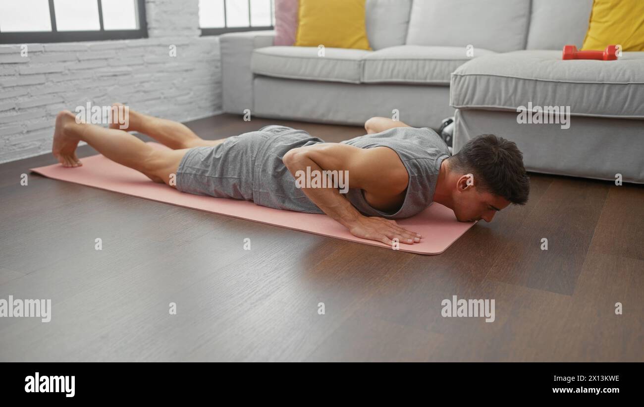 A fit hispanic man does push-ups on a pink mat in a modern living room ...