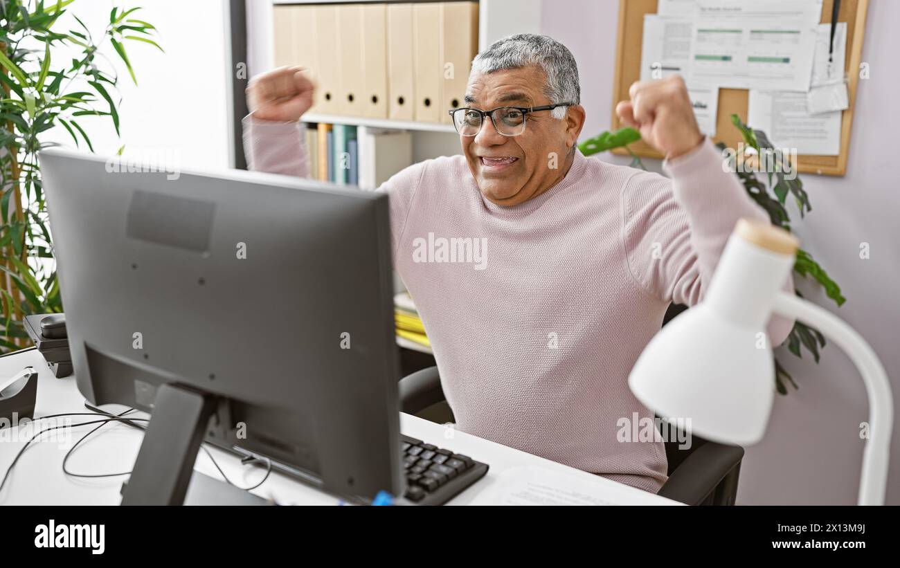 A cheerful middle-aged man celebrates success at his office computer ...