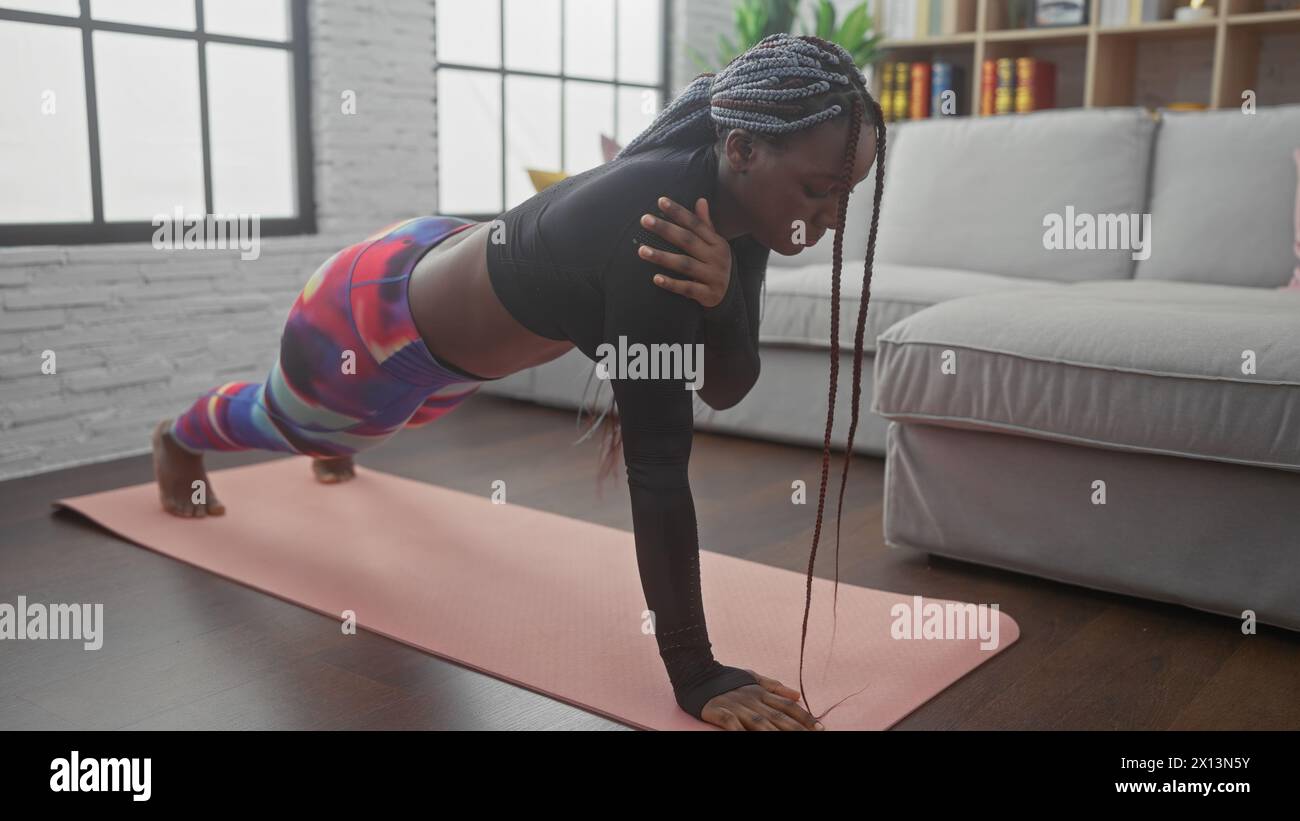 African american woman with braids performs push-up on yoga mat in her ...