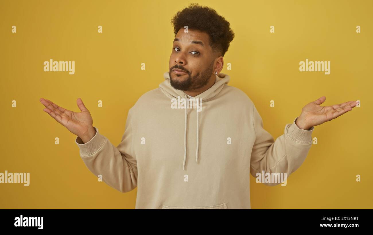 Confused african american man in hoodie against yellow background ...