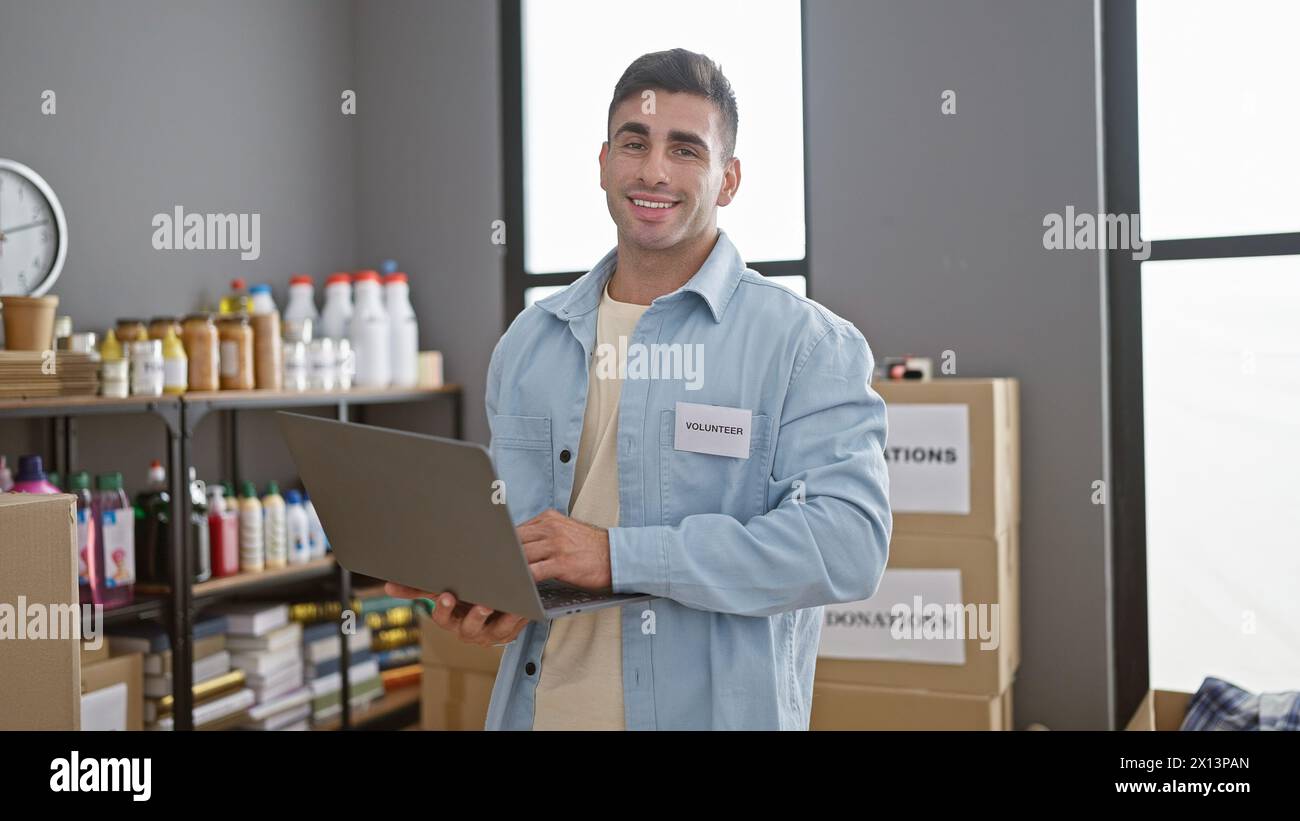 Young, confident hispanic man volunteers with a smile, using laptop at ...