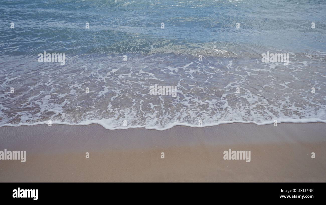 A tranquil beach scene captures the gentle lapping of foam-tipped waves ...