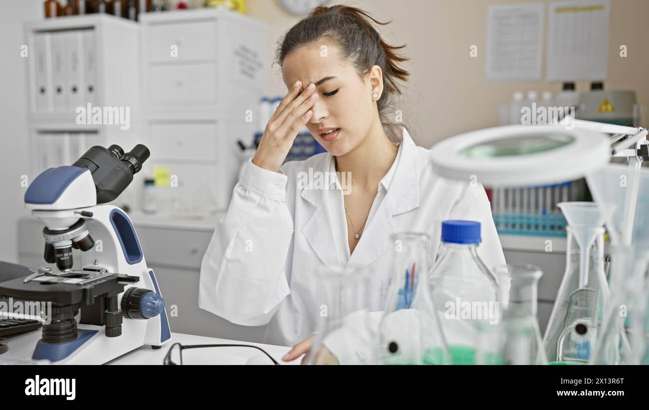 Stressed latina scientist woman in lab with microscope and equipment ...