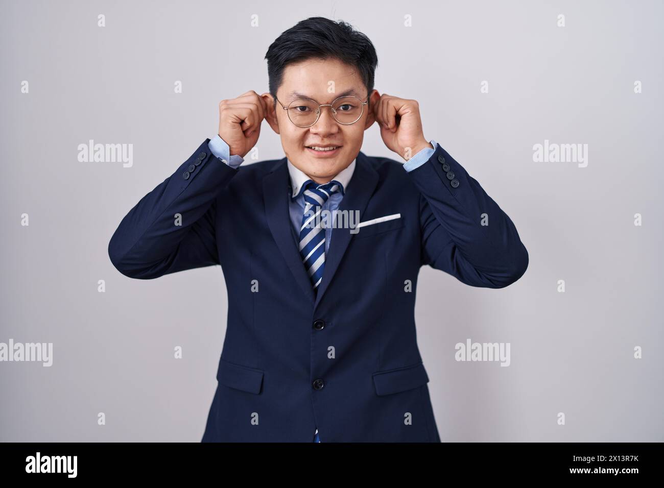 Young asian man wearing business suit and tie smiling pulling ears with ...