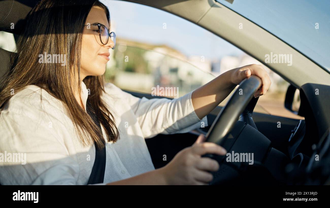 Young beautiful hispanic woman driving a car smiling wearing glasses on ...