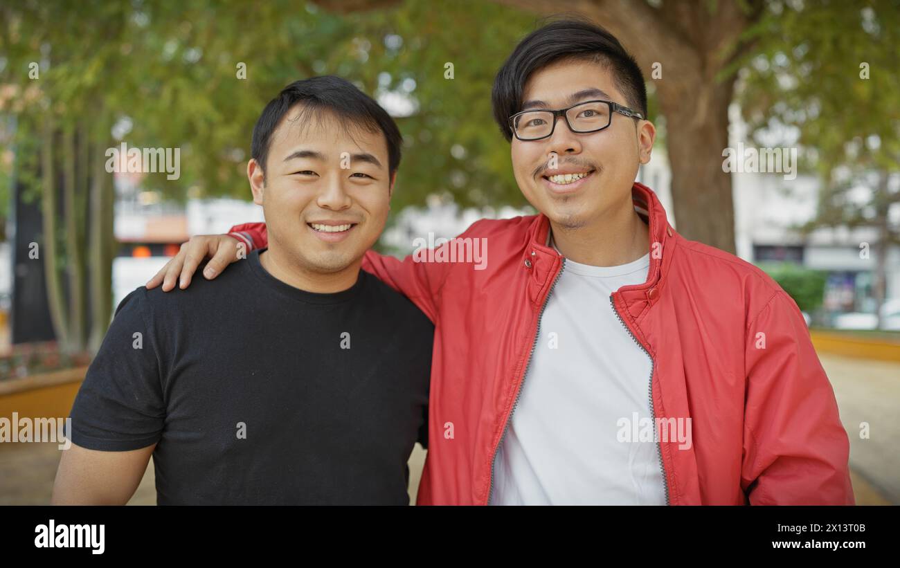Two asian men smiling together in a park setting with green trees in ...