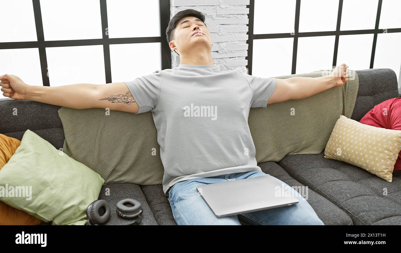 A relaxed asian man stretching on a sofa in a modern living room with ...