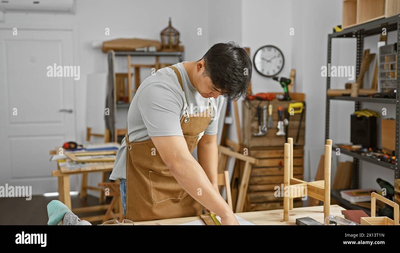A young asian man measuring wood in a well-organized carpentry workshop ...
