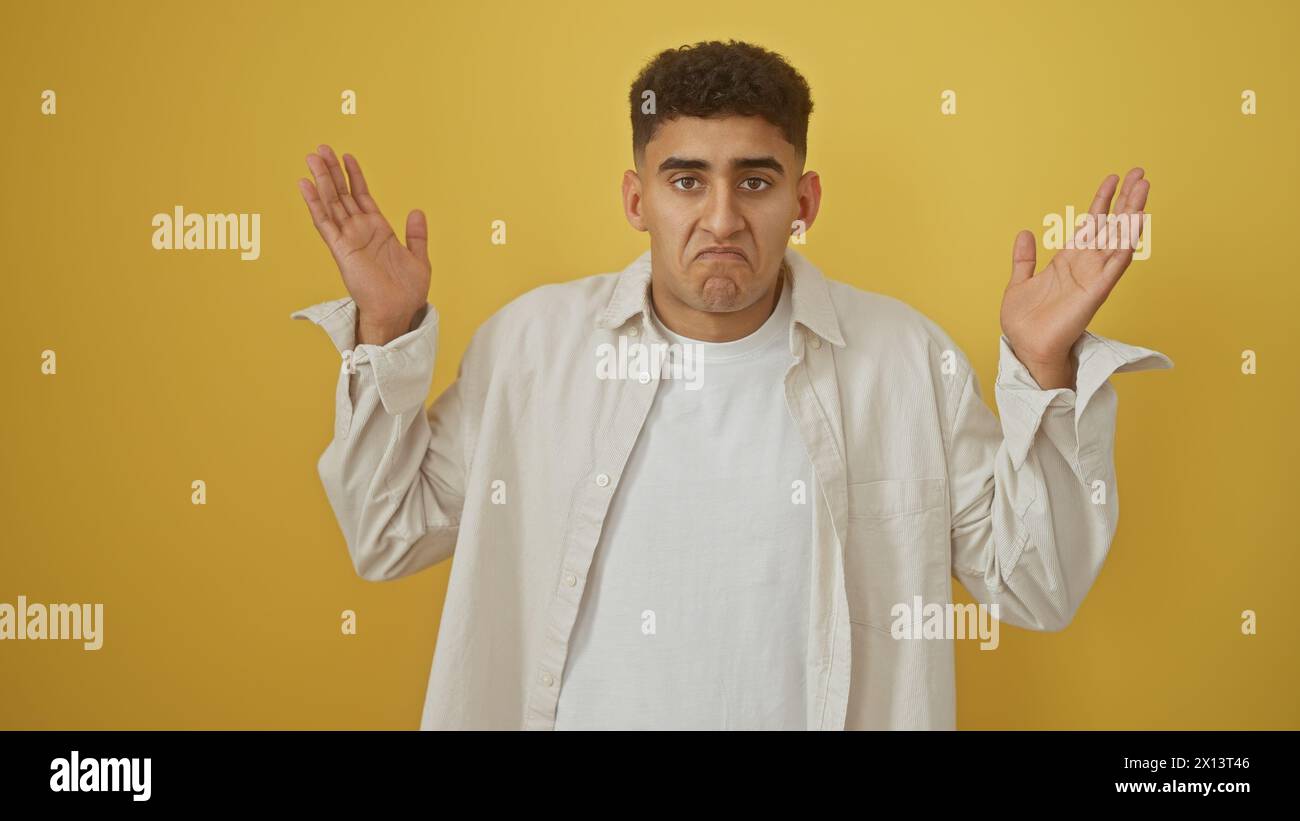 A confused young man shrugging against a yellow isolated background ...
