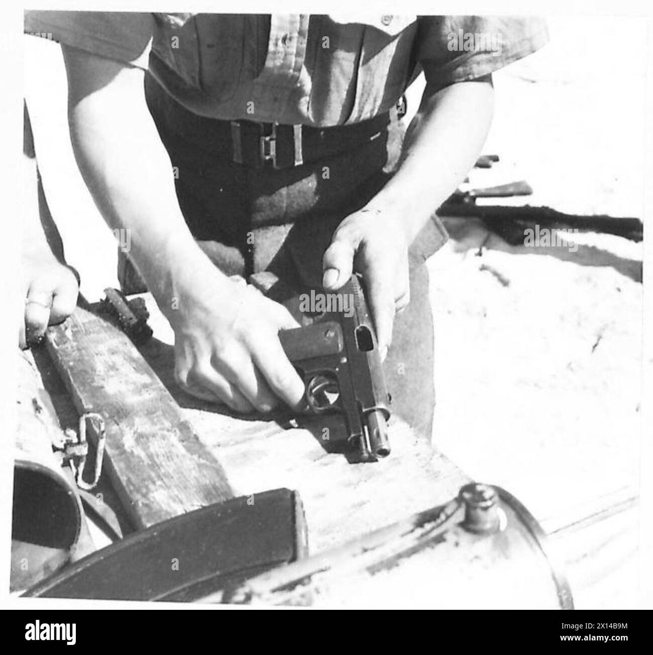 In a desert setting, a British Army armourer is inspecting a pistol ...