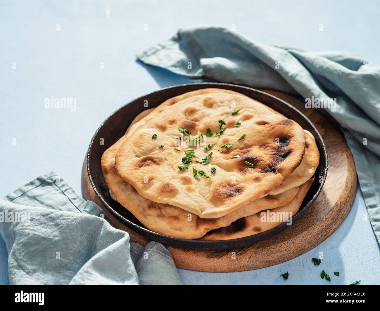 Stack of fesh naan breads in cast-iron pan on blue background with copy ...