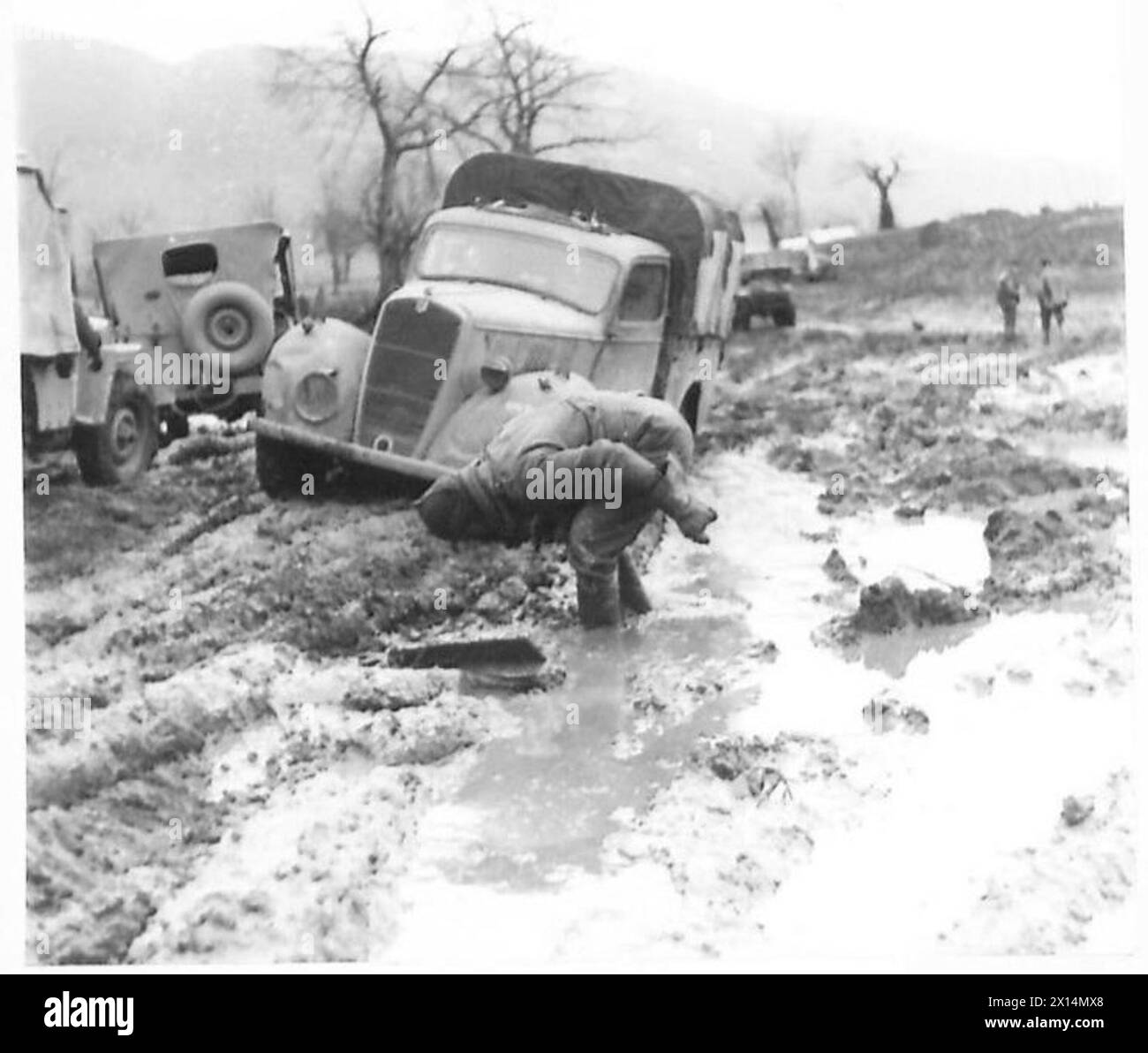 A truck bogged in mud is inspected by its driver to check for damage ...