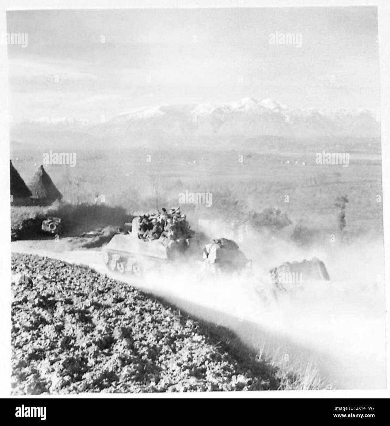 Sherman tanks, one towing a limber with an anti-tank gun and crew ...