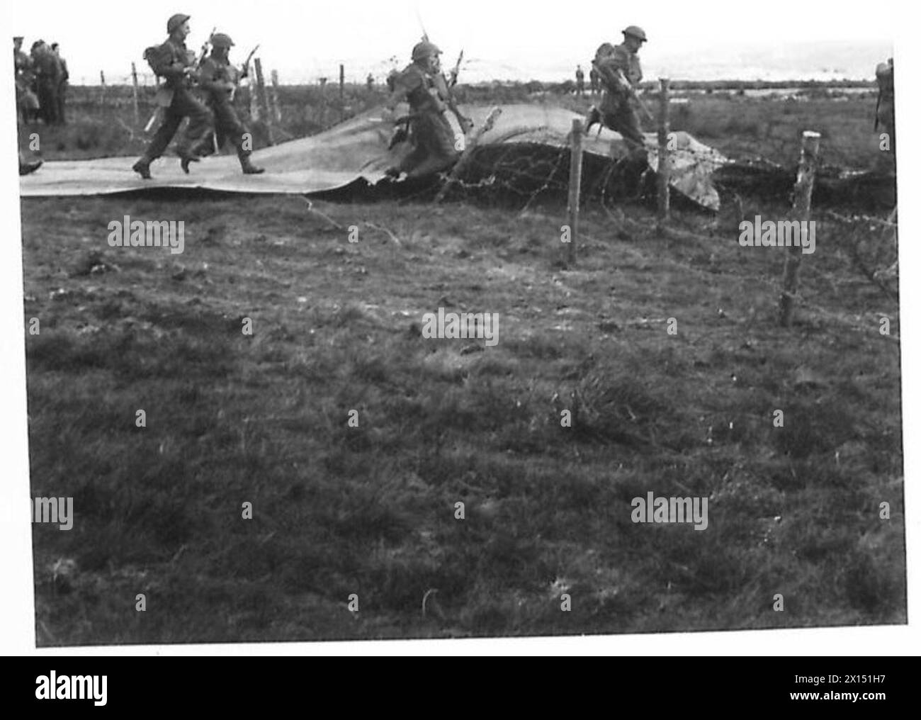 Infantry soldiers cross a wire obstacle using a mat deployed by a Bren ...