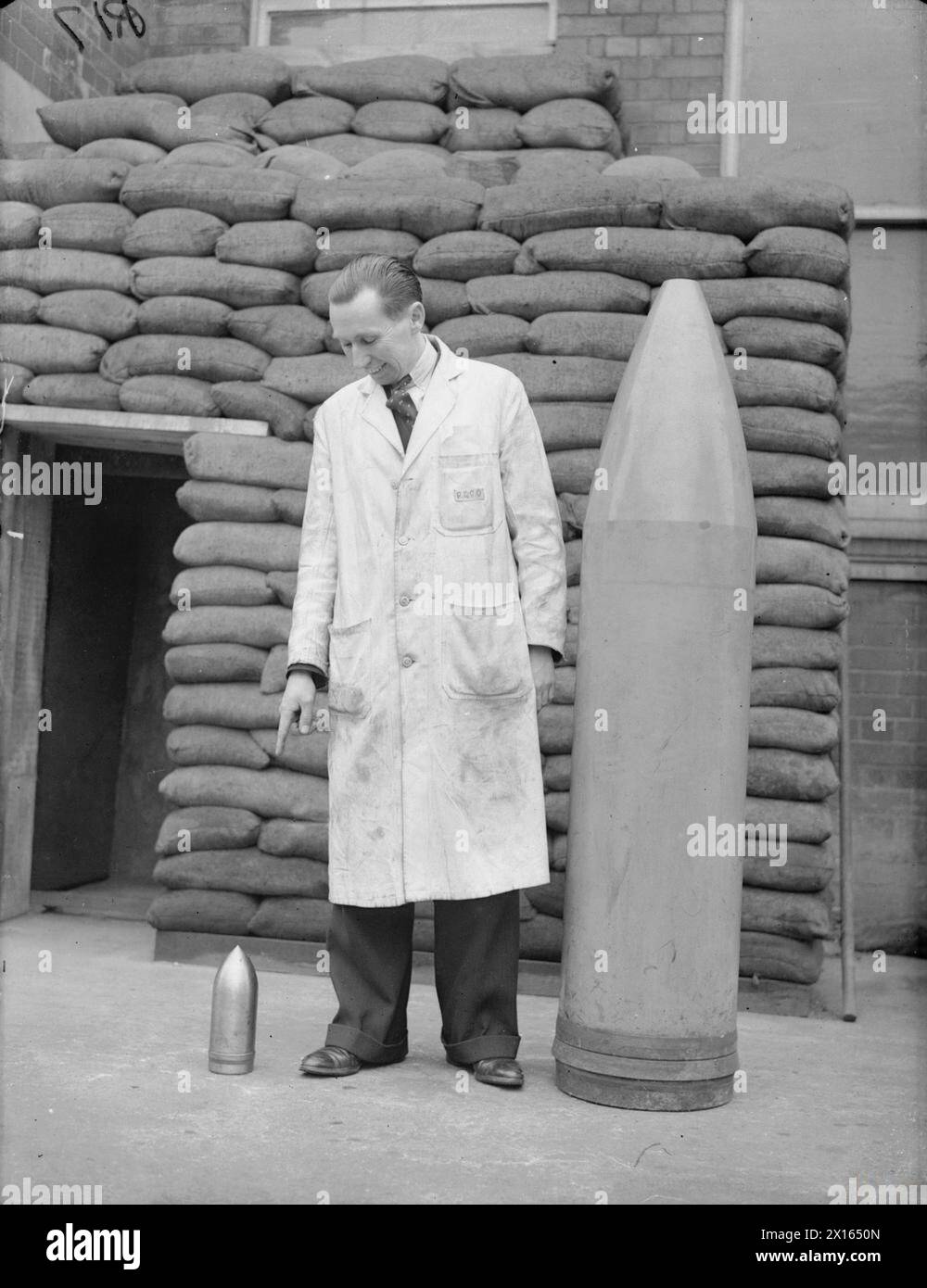 A munitions worker displaying the largest and smallest artillery shells ...