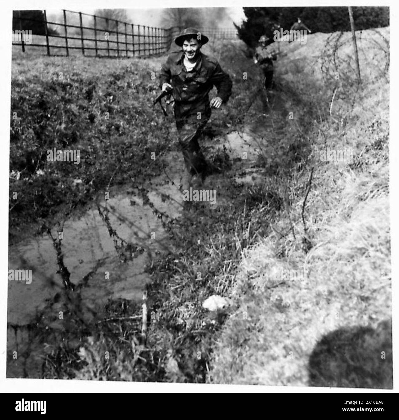 Soldiers advance through mud and wire obstacles during a battle drill ...
