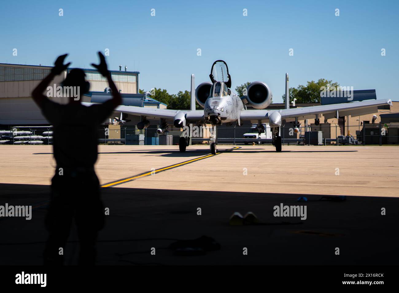 A man is standing in front of a jet, and the jet is on the runway. The ...