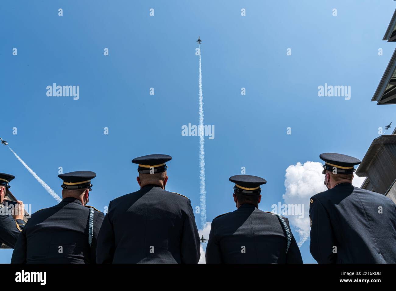 A group of men in military uniforms are watching a jet fly in the sky ...