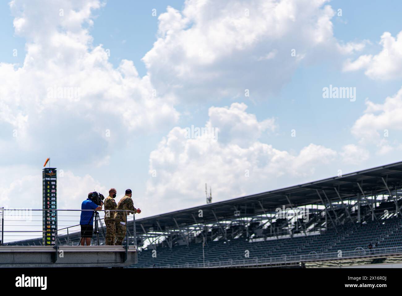 Three men standing on a bridge overlooking a stadium. The sky is cloudy ...