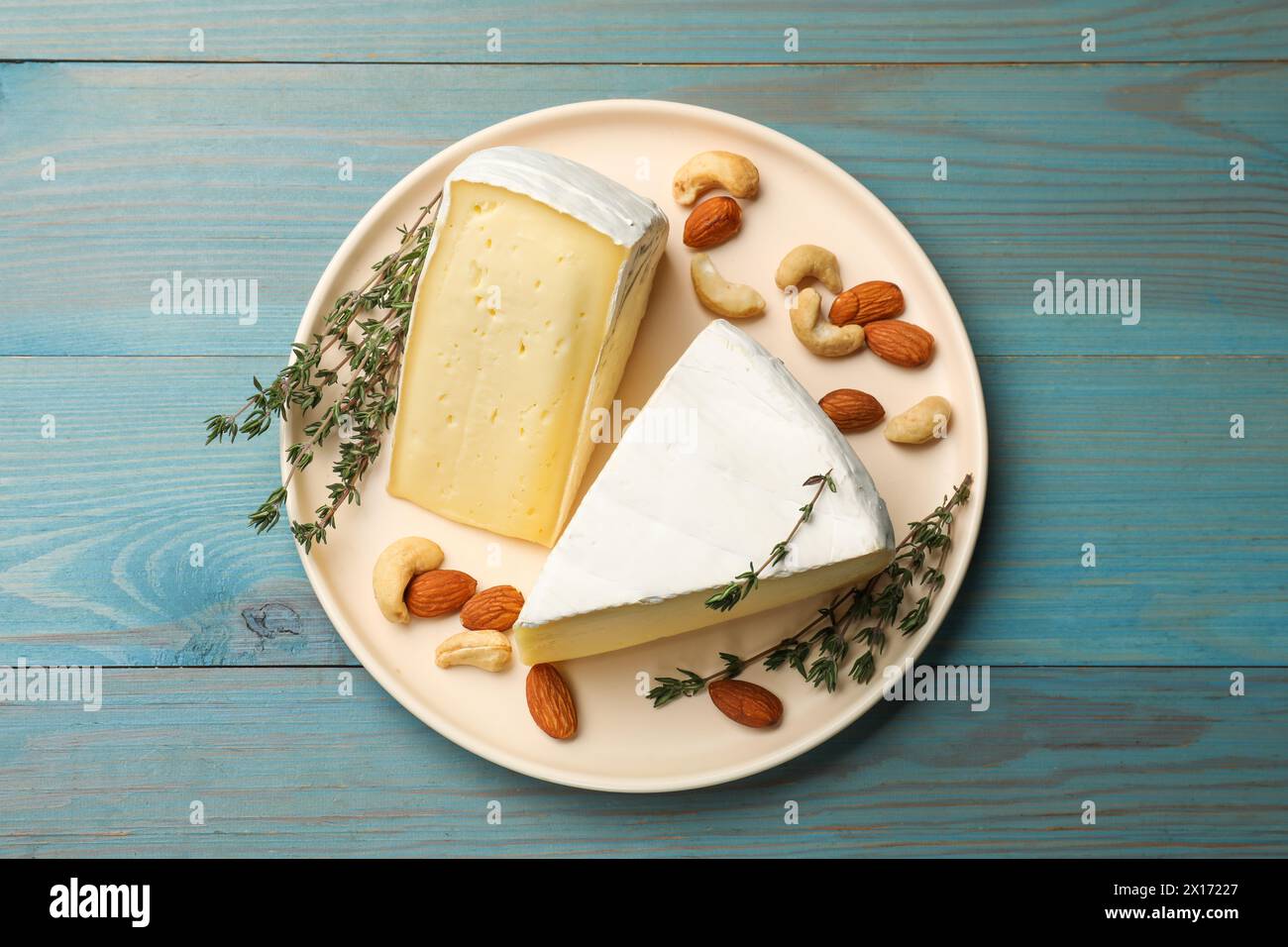Tasty Camembert cheese with thyme and nuts on light blue wooden table ...