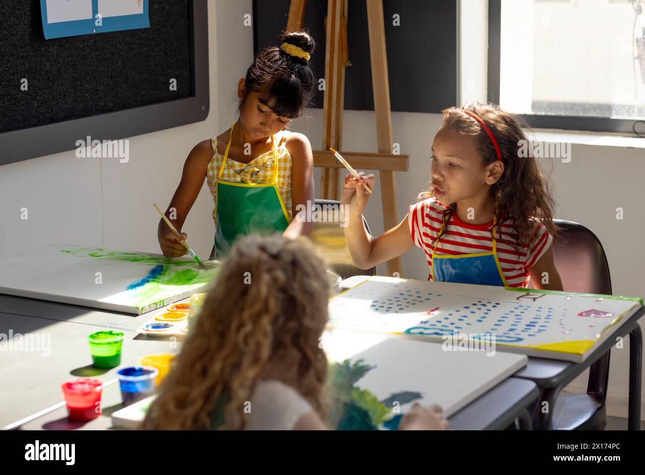 In school, during art class, diverse young students painting on canvas ...